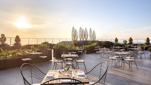 Restaurante no terraço com área externa, mesas e cadeiras, e vista para o pôr do sol.
