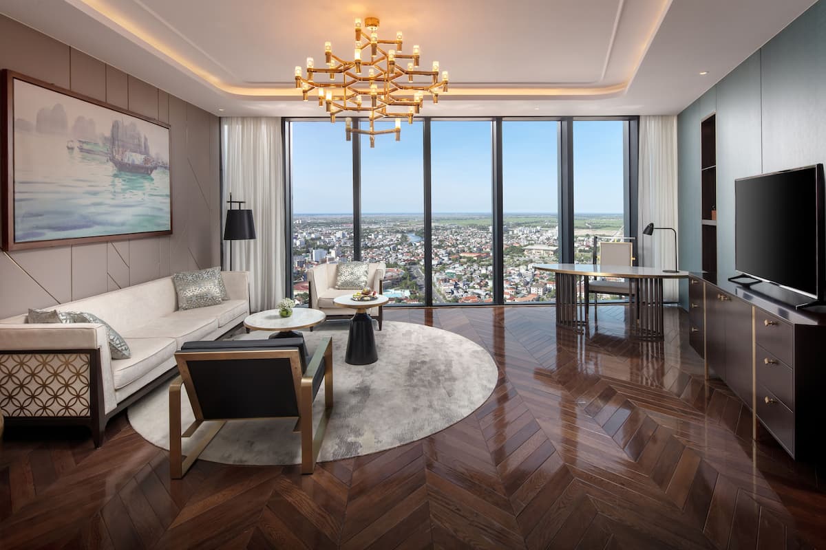 Sala de estar ampla com uma grande janela que oferece vista para a cidade, um lustre moderno e uma televisão de tela plana.