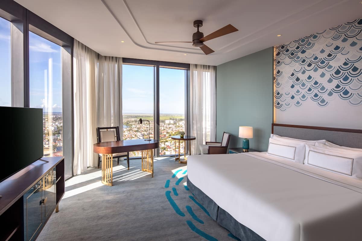 Quarto de hotel moderno com uma cama grande, uma escrivaninha e uma televisão.
