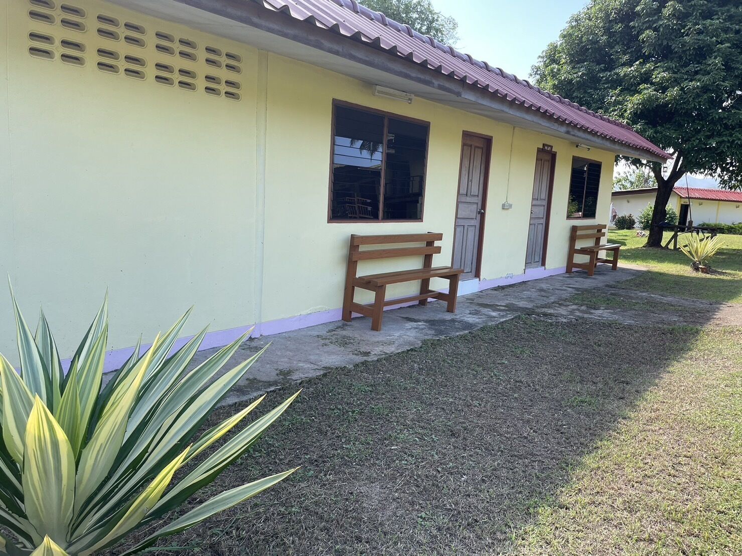 Um edifício com fachada amarela, teto vermelho e um pequeno alpendre com dois bancos de madeira.