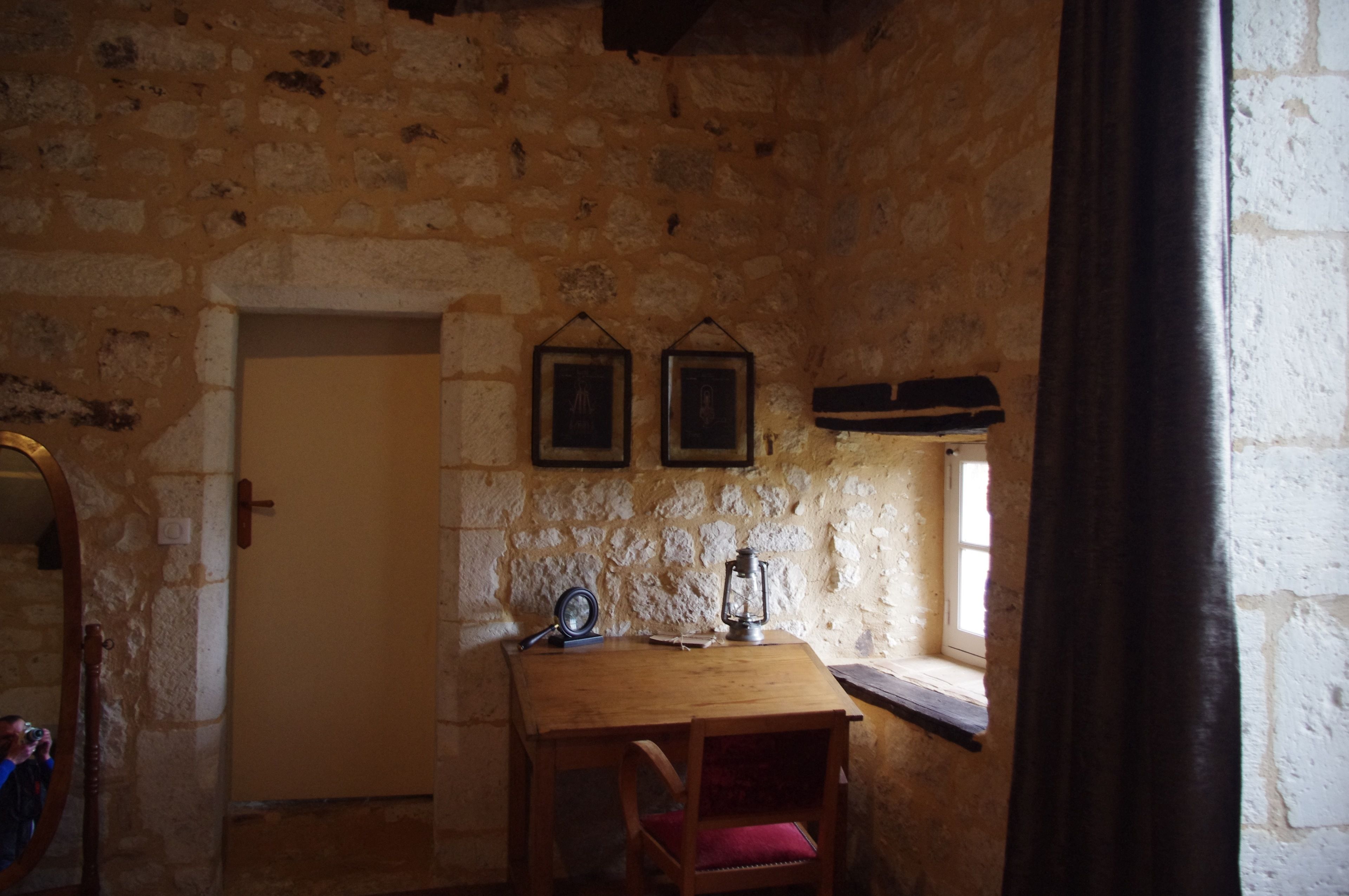 Quarto rústico com paredes de pedra, uma mesa de madeira, uma cadeira e uma janela com vista.