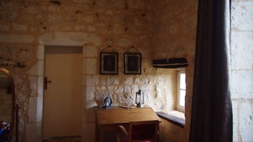 Quarto rústico com paredes de pedra, uma mesa de madeira, uma cadeira e uma janela com vista.