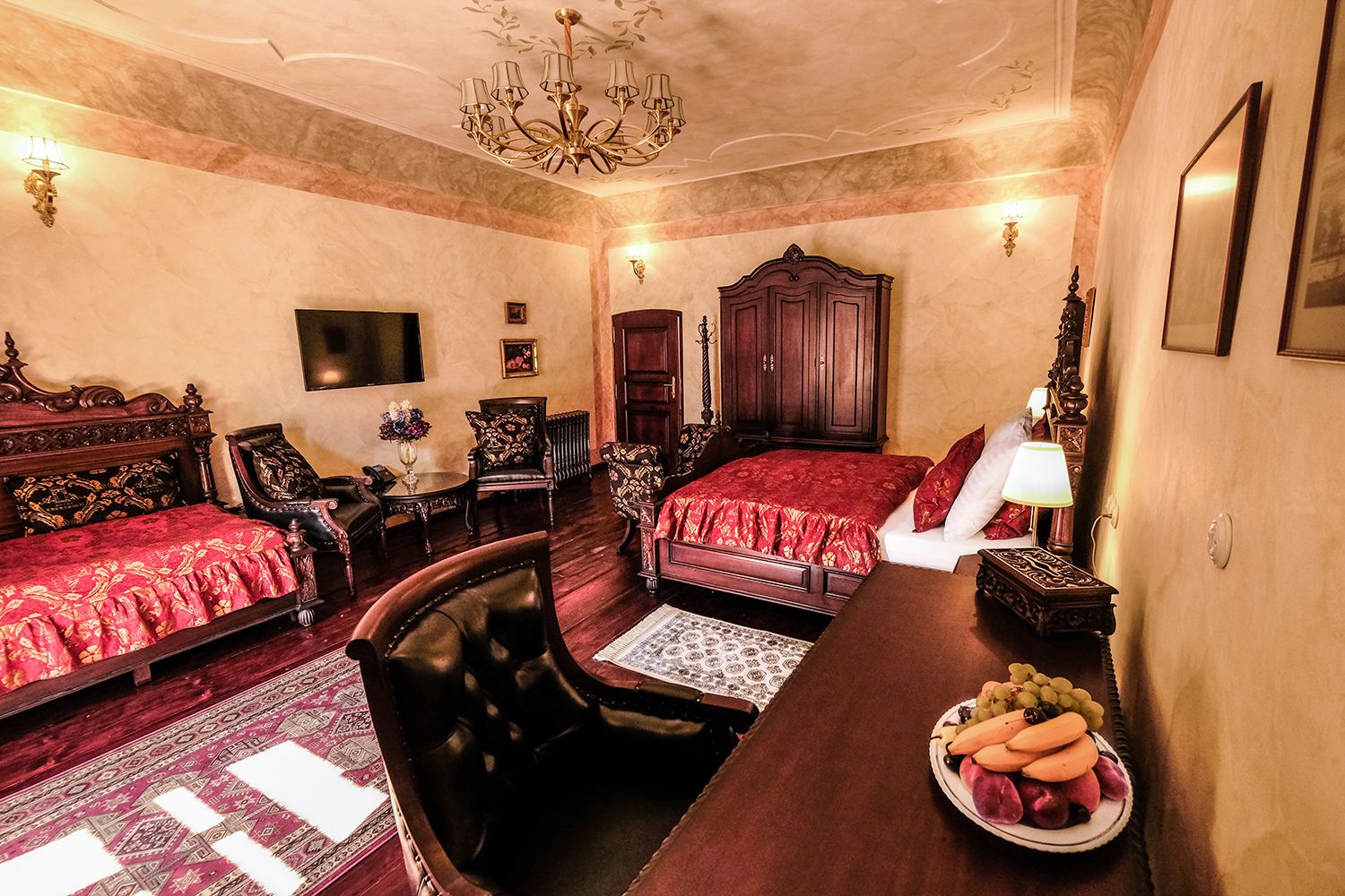 Quarto de hotel com duas camas, um guarda-roupa de madeira, uma escrivaninha com uma fruteira e um candelabro.