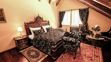 Quarto com cama grande, mesa de cabeceira, cadeira, mesa com vaso e janela com cortinas.