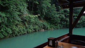 Uma mesa de madeira com um copo e uma caixa, com vista para um rio e vegetação densa.