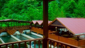 Um deck de madeira com vista para um rio e uma ponte, cabanas de madeira com telhados vermelhos e um corrimão de madeira.