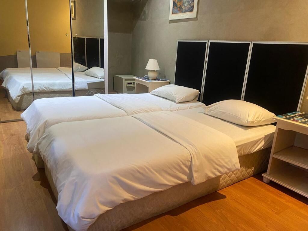 Quarto de hotel com duas camas, uma mesa de cabeceira com luminária e um espelho.