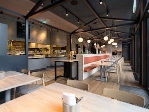 Interior moderno de restaurante com área de bar, assentos e cozinha à vista.