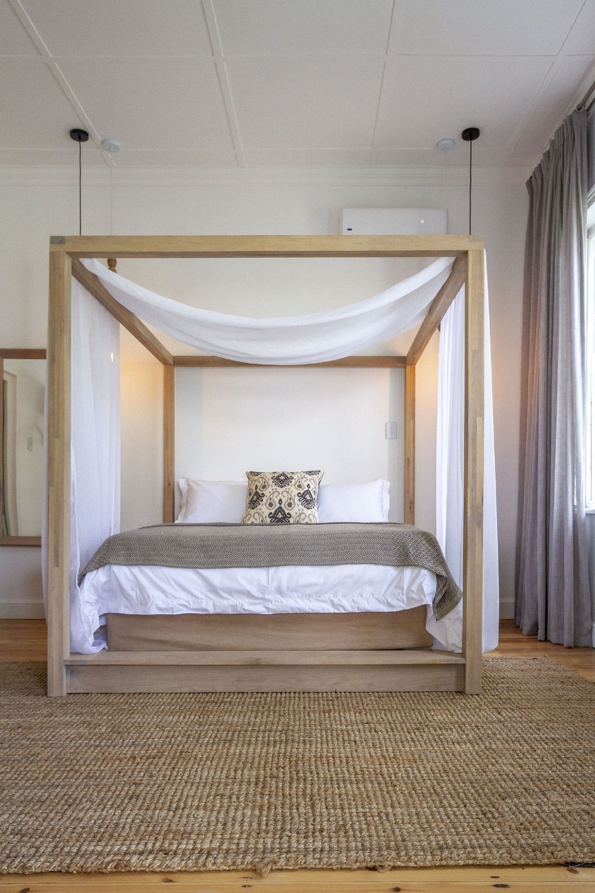 Uma cama com estrutura de madeira e dossel, um tapete tecido e uma janela com cortinas.