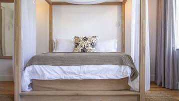 Uma cama com estrutura de madeira e dossel, um tapete tecido e uma janela com cortinas.