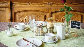 Disposição para o café da manhã com uma mesa posta para dois, incluindo pratos, xícaras, um bule e uma placa com a inscrição 'Guten Morgen'.