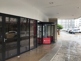 Entrada de um hotel com porta giratória, portas de vidro e calçada de azulejos.
