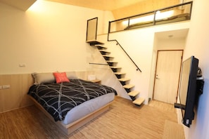 Quarto com uma cama, televisão, escada e porta.