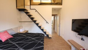 Quarto com cama, televisão, um banco de madeira, escadas e uma televisão na parede.