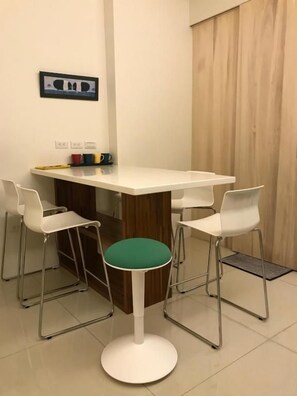 Uma pequena área de refeições com uma mesa branca e quatro cadeiras brancas, uma delas com almofada verde no assento.