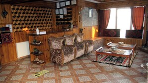 Quarto com piso estampado, paredes de madeira, sofá, mesa com uma tigela e janela com cortinas.