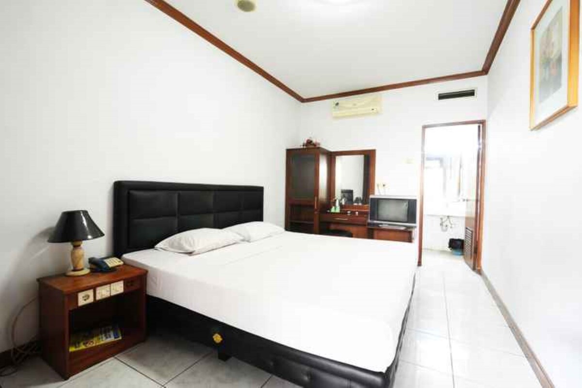 Quarto com cama, mesa de cabeceira, luminária e televisão.
