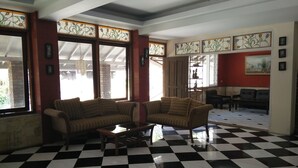 Um quarto com chão quadriculado, dois sofás listrados, uma mesa pequena e uma parede vermelha com quadros emoldurados.