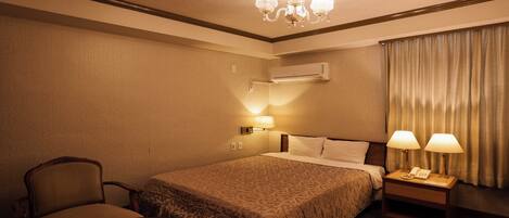 Quarto de hotel com cama, mesa de cabeceira com abajur, cadeira, aparelho de ar condicionado e lustre.