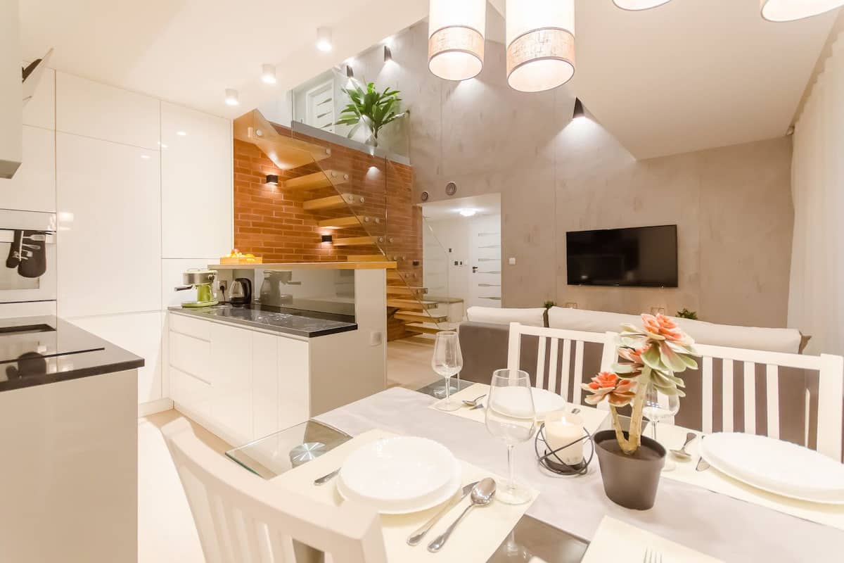 Uma cozinha moderna com ilha central, armários brancos e parede decorada com tijolos.