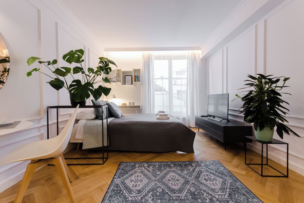 Quarto moderno com uma cama, uma escrivaninha, uma cadeira, uma televisão e duas plantas em vasos.