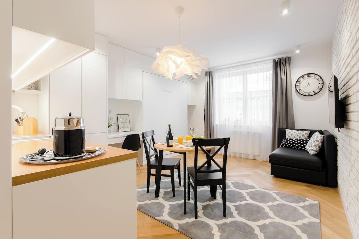 Uma sala de estar moderna com área de refeições, um sofá preto, um relógio e uma janela grande com cortinas.
