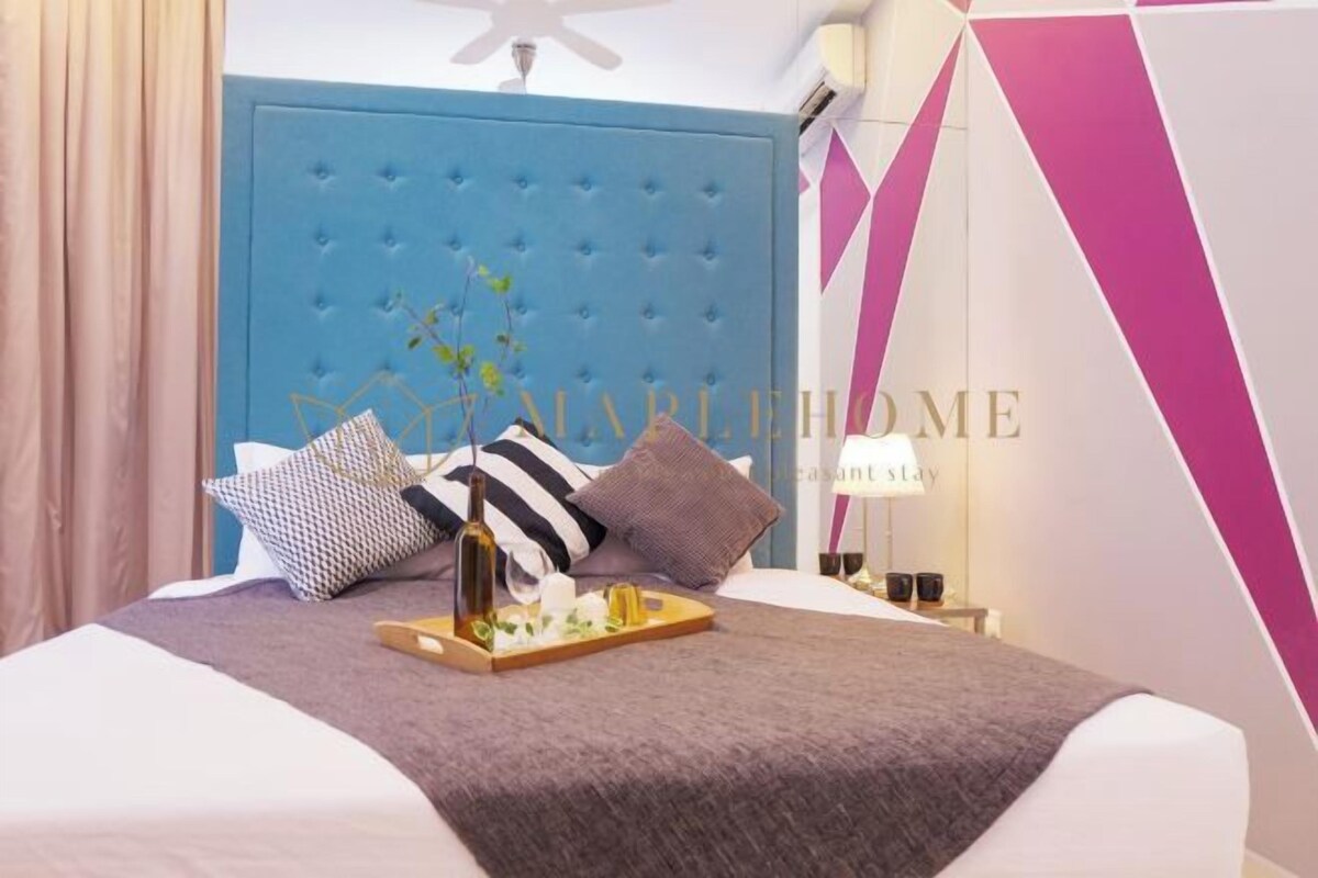 Quarto de hotel moderno com cabeceira estofada, mesa de cabeceira com luminária e bandeja com garrafa e copos.