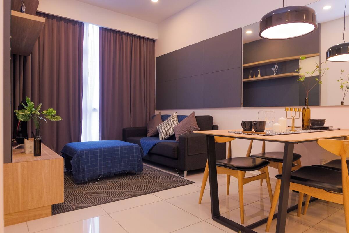 Quarto moderno com cama, sofá, mesa de jantar com cadeiras, escrivaninha pequena e um espelho grande.
