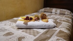 Uma cama com colcha estampada, um travesseiro decorativo e um pequeno arranjo de flores secas e uma fruta sobre a cama.