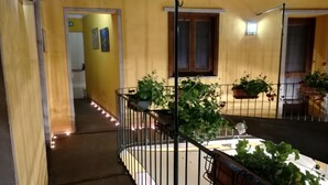 Uma varanda com plantas em vasos, guarda-corpo de madeira e vista para o interior do edifício.