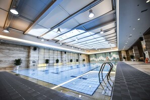 Piscina interior com chão em azulejo, iluminação pendente e teto de vidro.