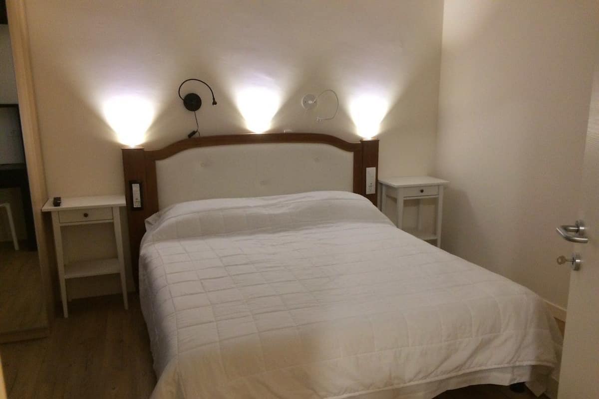 Uma cama bem arrumada com cabeceira de madeira e duas mesas de cabeceira, cada uma com uma luminária.
