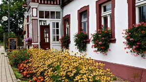 Um edifício com fachada branca e molduras de janela vermelhas, rodeado por um jardim com flores amarelas e vermelhas.