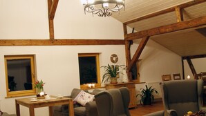 Um loft espaçoso com vigas de madeira aparentes, um candelabro e um espaço de estar acolhedor com uma mesa e cadeiras.