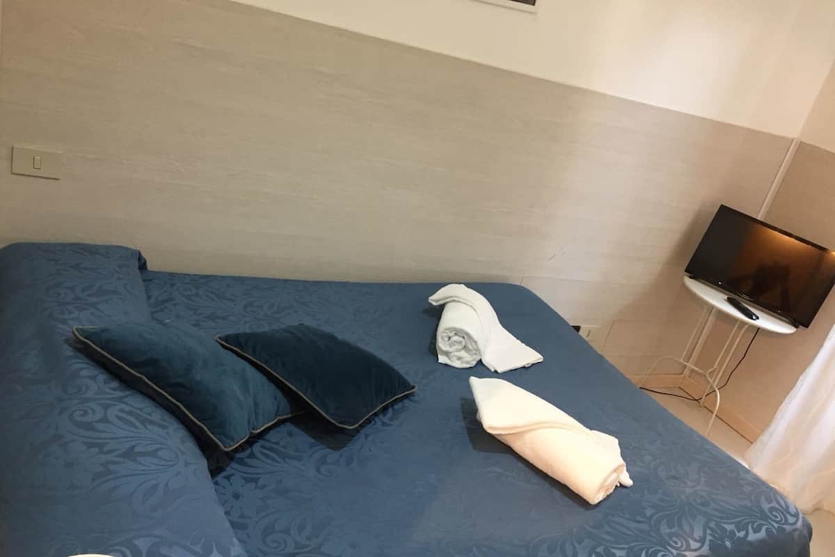 Quarto de hotel com cama, almofadas, televisão e toalha.