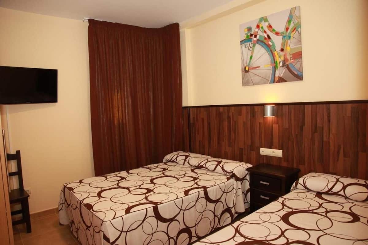 Quarto de hotel com duas camas, televisão, cabeceira de madeira e um quadro na parede.