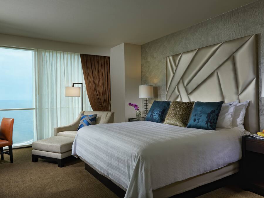 Quarto de hotel com uma cama grande, um sofá, uma escrivaninha e vista para o oceano.
