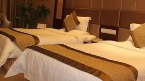 Quarto de hotel com duas camas, uma cabeceira grande e acolchoada, uma planta e um quadro na parede.