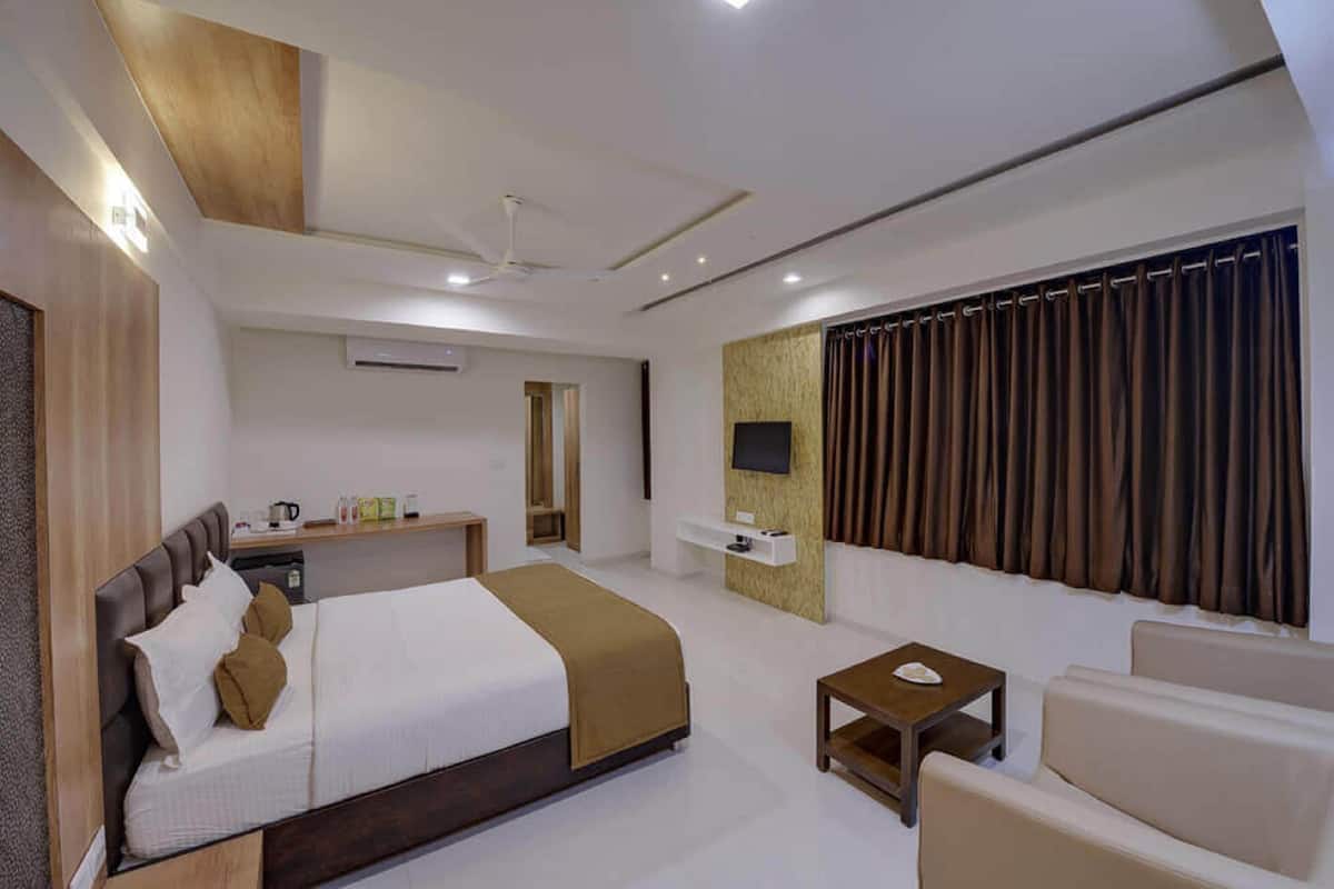 Quarto de hotel moderno com uma cama grande, um sofá, uma mesa pequena, uma TV e um ventilador de teto.