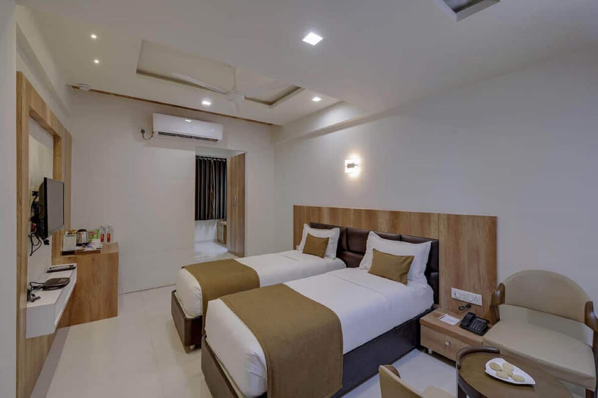 Quarto de hotel com duas camas, uma escrivaninha com computador, uma cadeira, mesa de cabeceira com telefone e unidade de ar condicionado.
