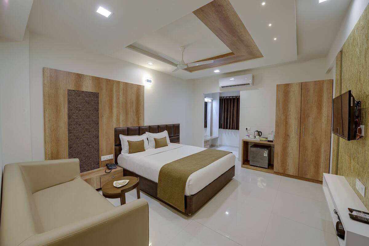 Quarto de hotel moderno com uma cama grande, um sofá, uma mesinha e uma televisão.