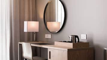 Quarto de hotel moderno com escrivaninha de madeira, uma cadeira, um espelho redondo e uma mesinha de cabeceira com chaleira.