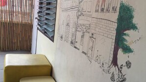 Quarto com um mural de um edifício e uma árvore, um banco de madeira e uma mesa pequena.