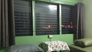 Quarto com duas camas, uma mesinha com toalha de mesa florida e uma janela com persianas.