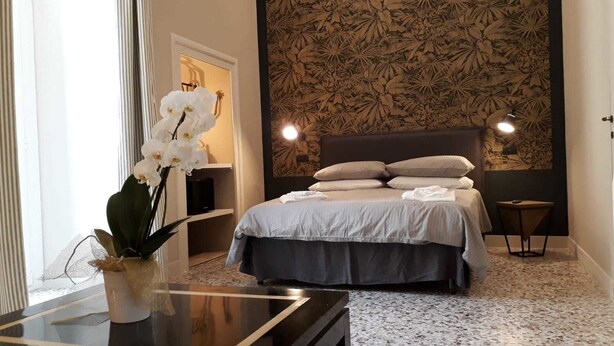 Um quarto com uma cama, uma mesa de cabeceira, um vaso com flores e uma parede com padrão floral.