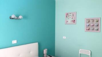 Quarto com paredes verde-água, uma cama branca, uma mesa de cabeceira com abajur e uma cadeira.