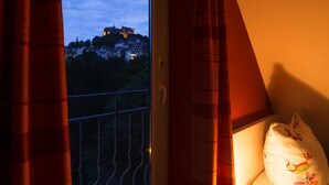 Quarto com vista para um edifício no topo da colina, cortinas e travesseiro.