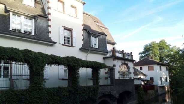 Um edifício histórico com fachada branca, janelas em arco e uma ponte sobre um canal.