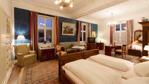 Quarto de hotel tradicional com duas camas, uma escrivaninha, uma cadeira, uma televisão e uma janela grande com cortinas.