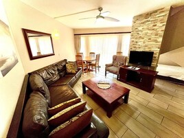 Uma sala de estar com sofá de couro, mesa de centro, televisão e canto de jantar com cadeiras e mesa.